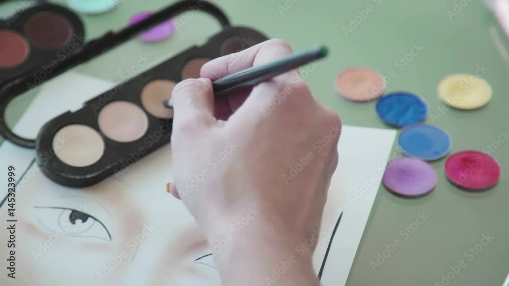 Young woman in a bright studio draws a facechart. The make-up artist ...