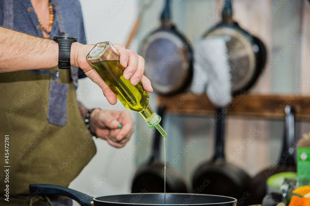 Chef in restaurant kitchen at stove with pan adding oil. Stock Photo ...