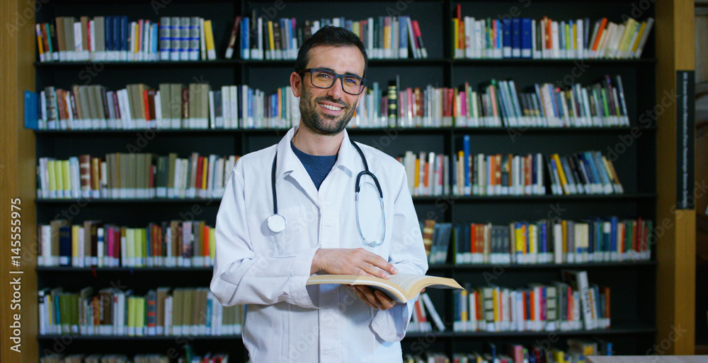 A young and beautiful doctor in a library smiling happy and holding ...