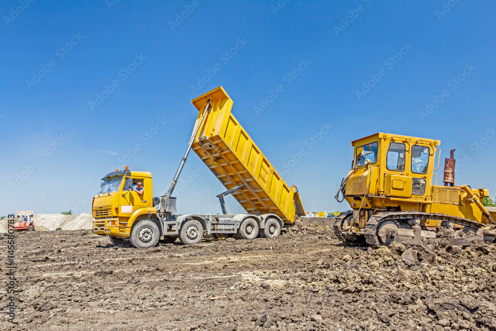Heavy earthmover is moving earth at building site. Dump truck is ...