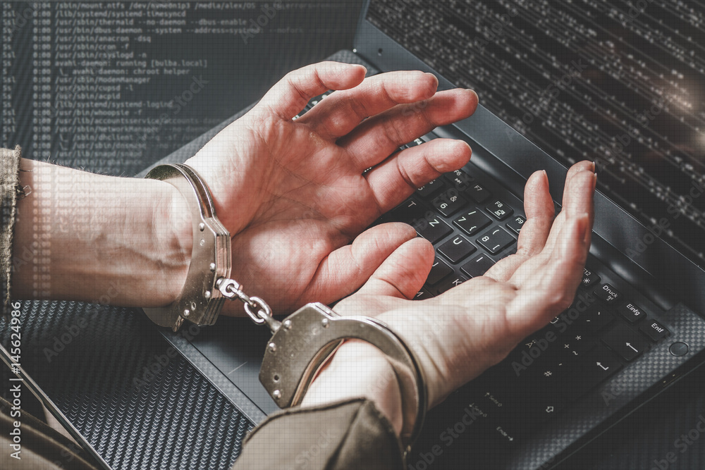 Arrested hacker with hands behind in handcuffs on the laptop keyboard ...