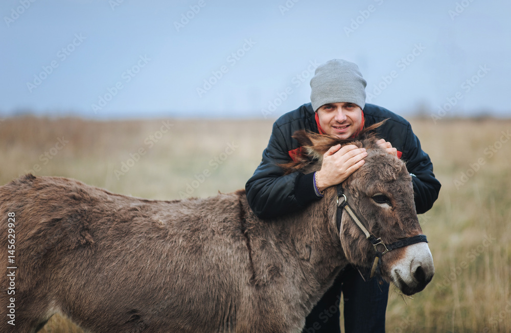 The young man sits near the donkey. Friendship between man and animal ...