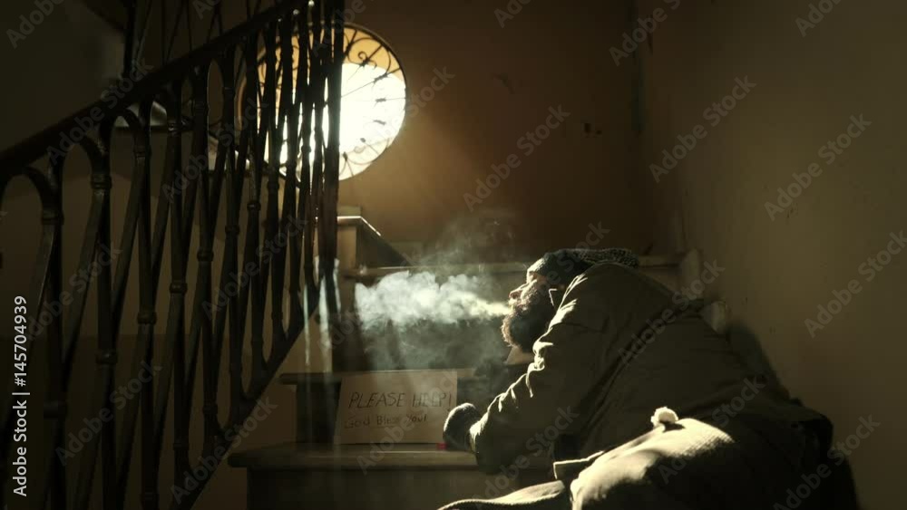 Homeless smokes a cigarette looking at the light, lying on the stairs ...
