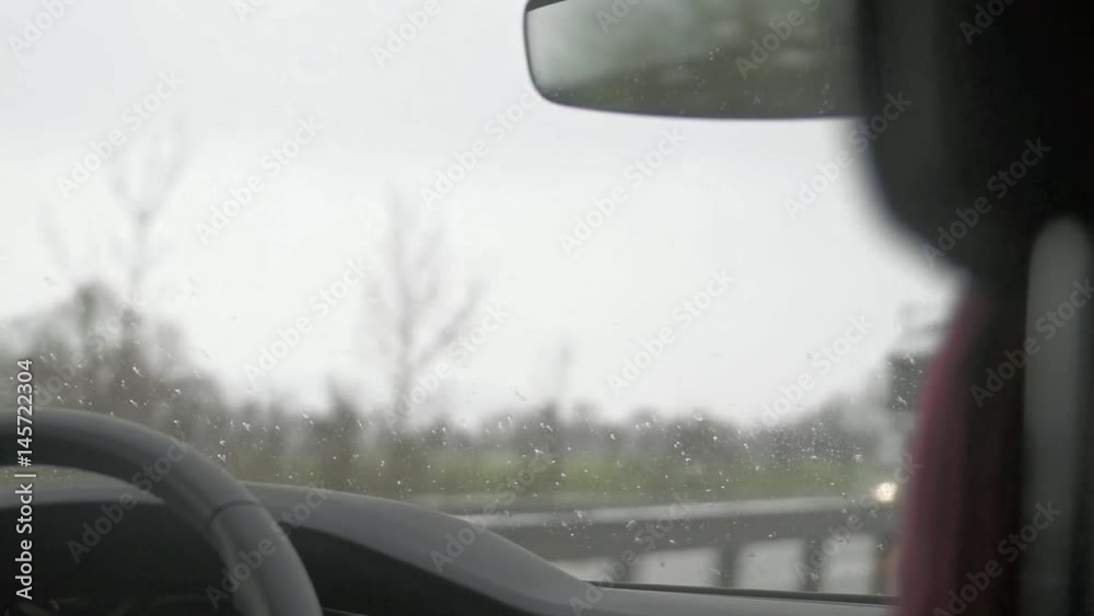 A car is driving on a highway in the rain; rain splatters on the car ...
