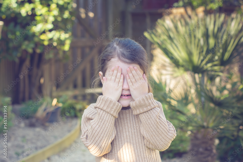 Little girl playing hide and seek in the garden, holding her hands in ...