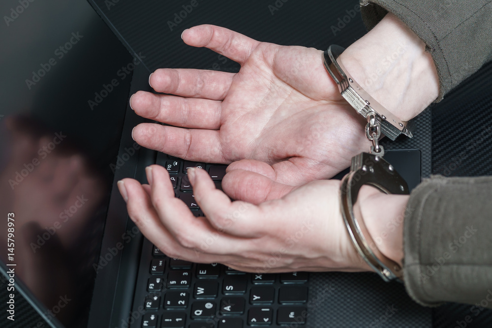 Arrested hacker with hands in handcuffs on the laptop keyboard and ...