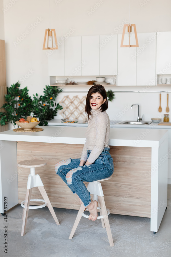 girl standing near the kitchen table in a high chair. Bright, white ...