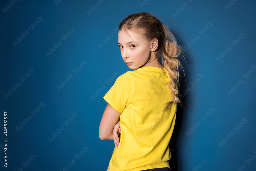 rear view of preteen girl in yellow shirt in studio isolated on blue ...