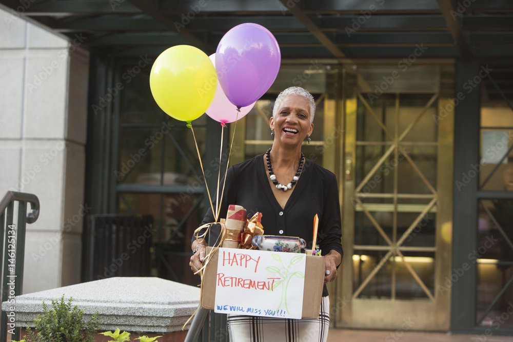 Black woman carrying belongings with happy retirement sign and balloons ...