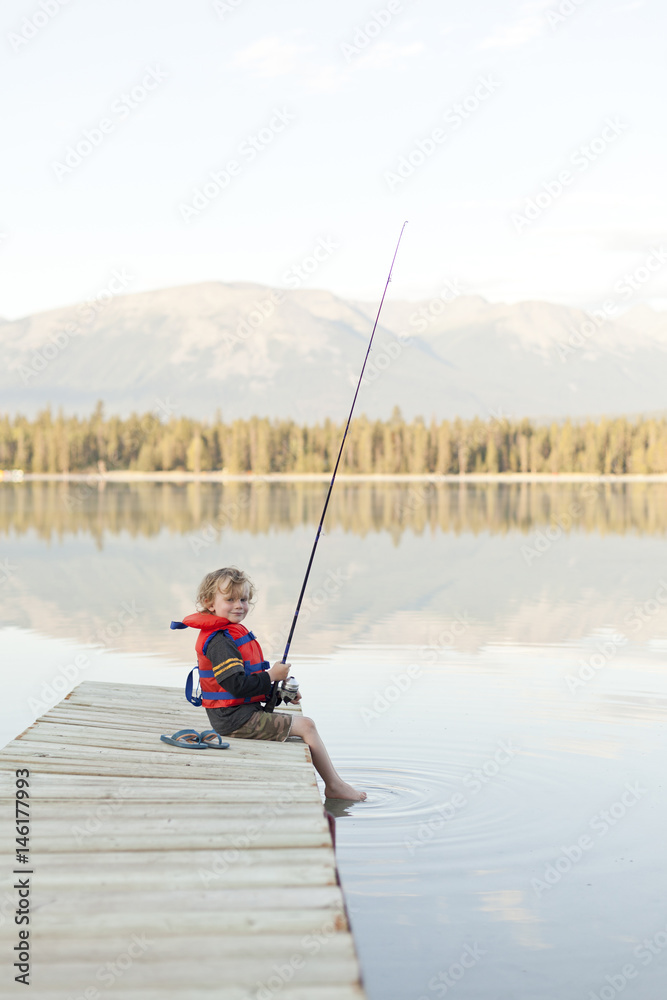 Caucasian boy sitting on dock at lake holding fishing rod Stock Photo ...
