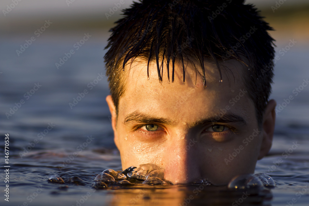 Portrait of young man sitting in the water at the sea. Half of face is ...