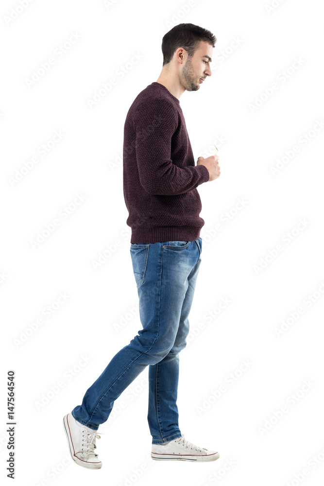 Side view of serious young man holding sunglasses walking and looking ...