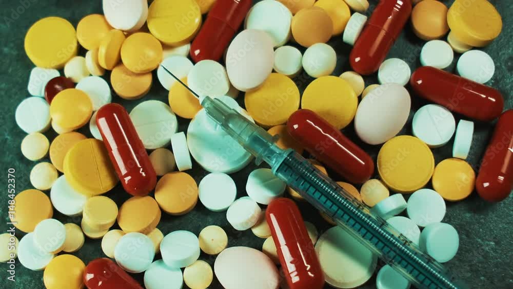 Many multi-colored tablets. Syringe with needle for injection ...