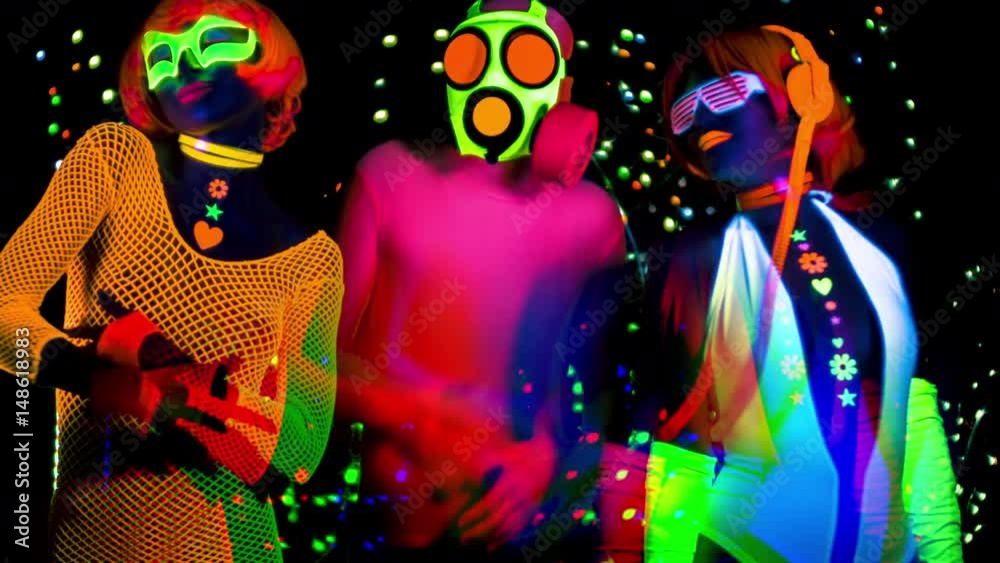 two female gogo ravers in fluorescent costume dancing with masked man ...
