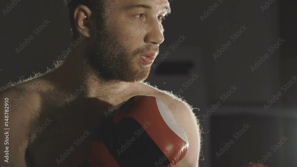 Close-up of kick in boxer's cheek with sweat's splatters in darkness ...