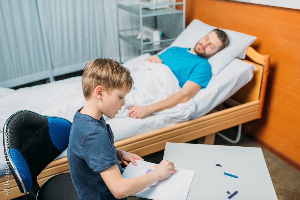 son drawing pictures while sick father laying on hospital bed at ward ...