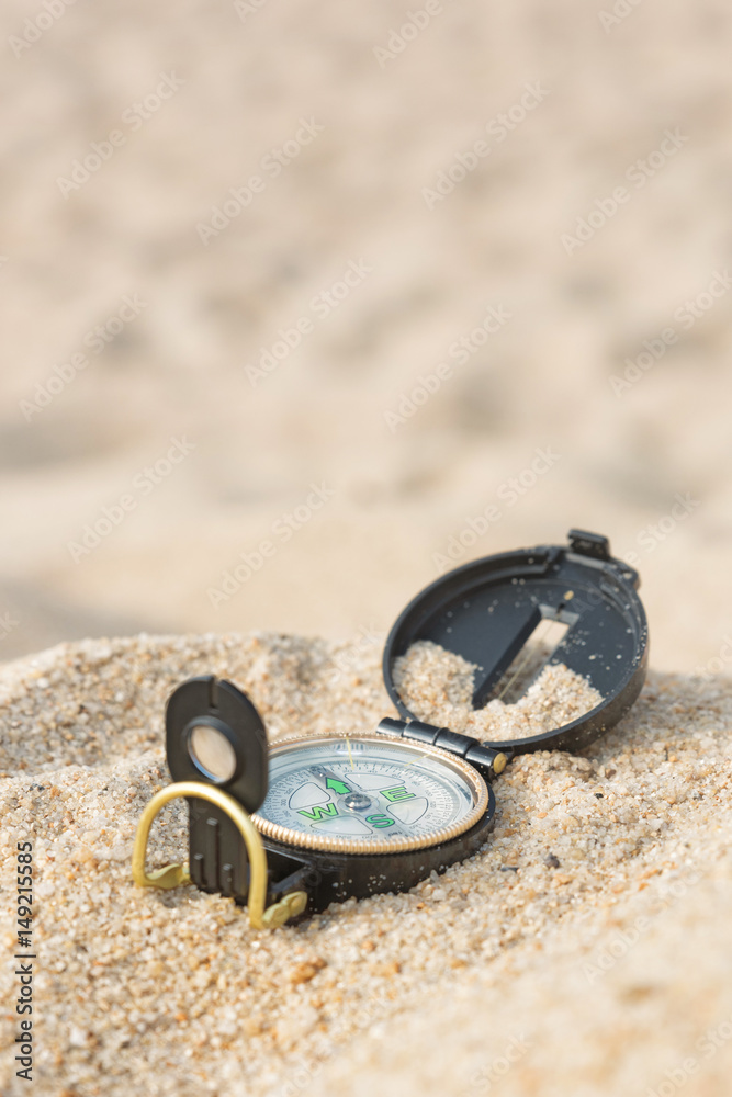 Compass in a beach sand. Compass lying on sea hot sand. Vertical view ...