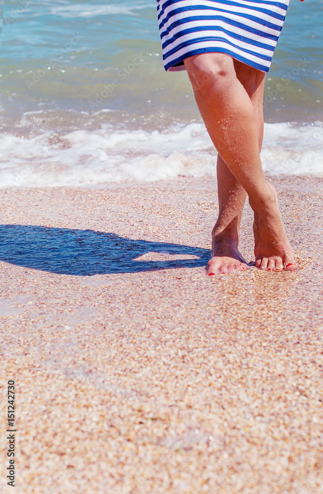 Foto de Female legs on the beach. Legs of a girl in a striped dress in ...