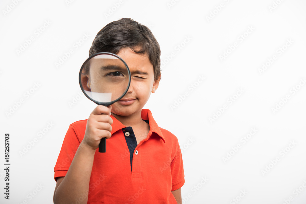 indian cute kid or small boy looking at camera through magnifying glass ...