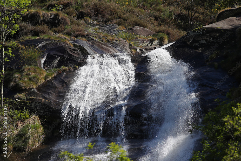 Water dripping down a tall mountain waterfall with lush vegetation ...