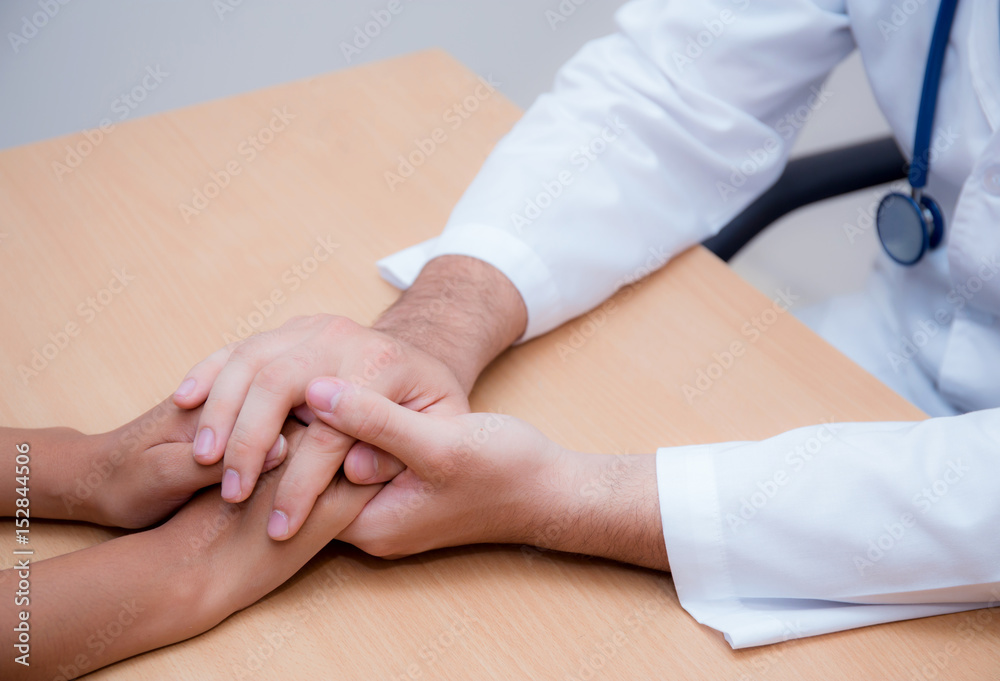 Friendly male doctor hand holding patient hand sitting at the desk for ...