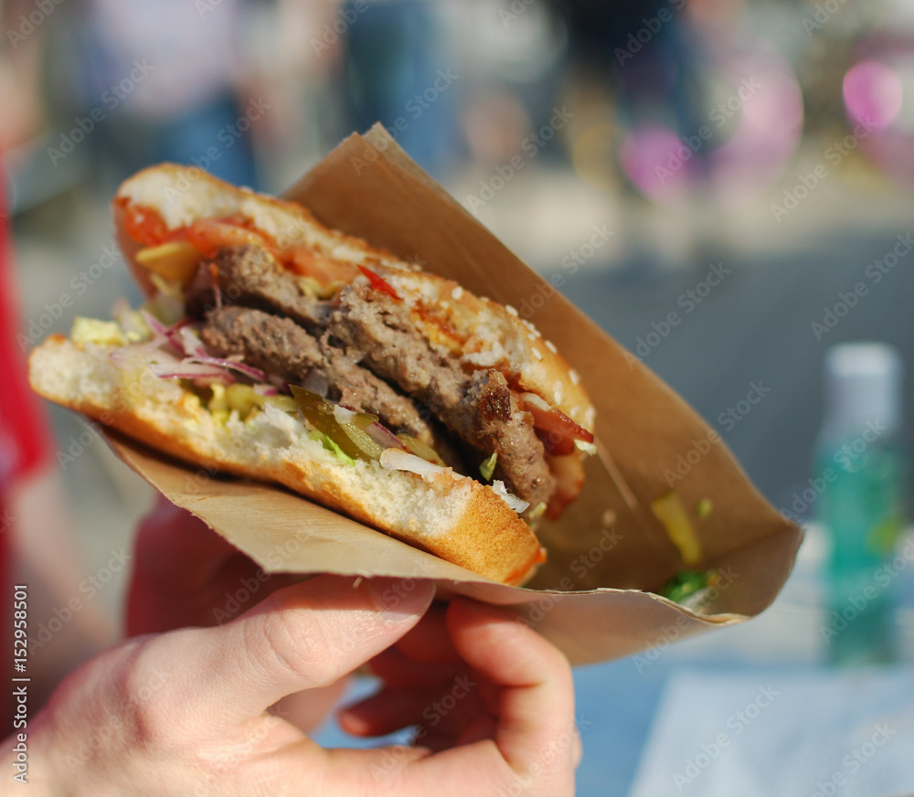 Man holding wrapped in paper bited burger on city background. Photos ...