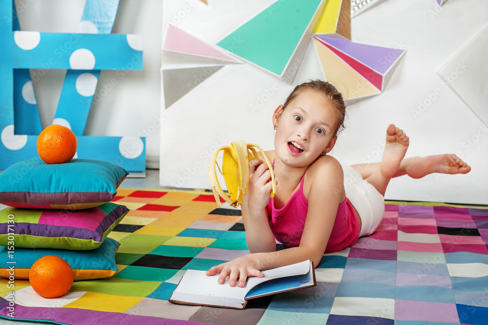 Little girl reading an interesting book and eating a banana. The ...