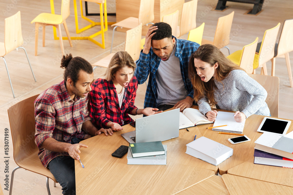 Sad confused students sitting in library using laptop computer. Stock ...