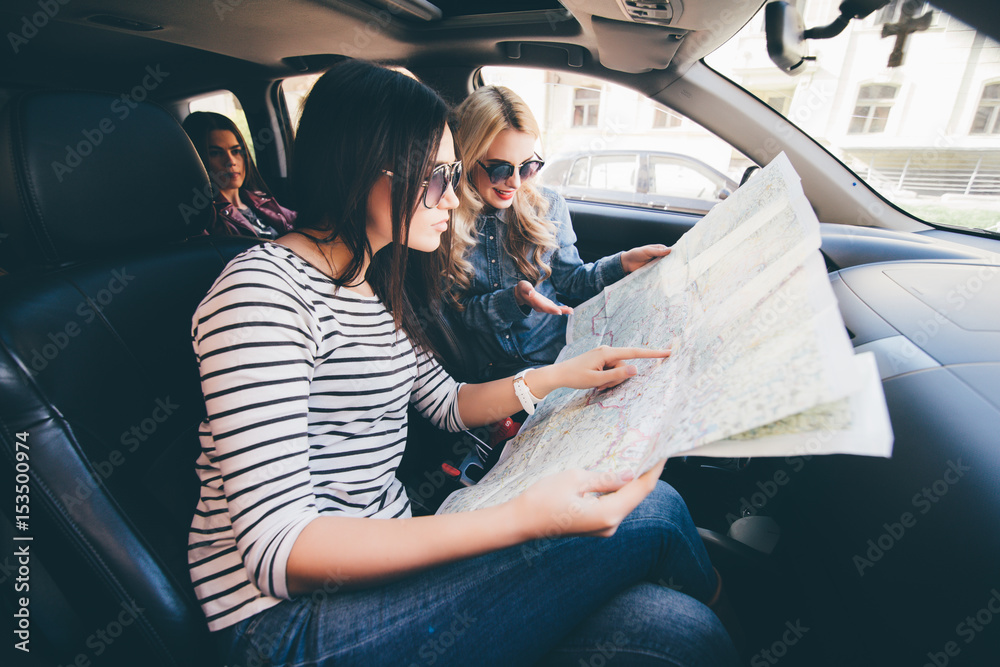 Women on vacation looking at map for directions while driving in car ...
