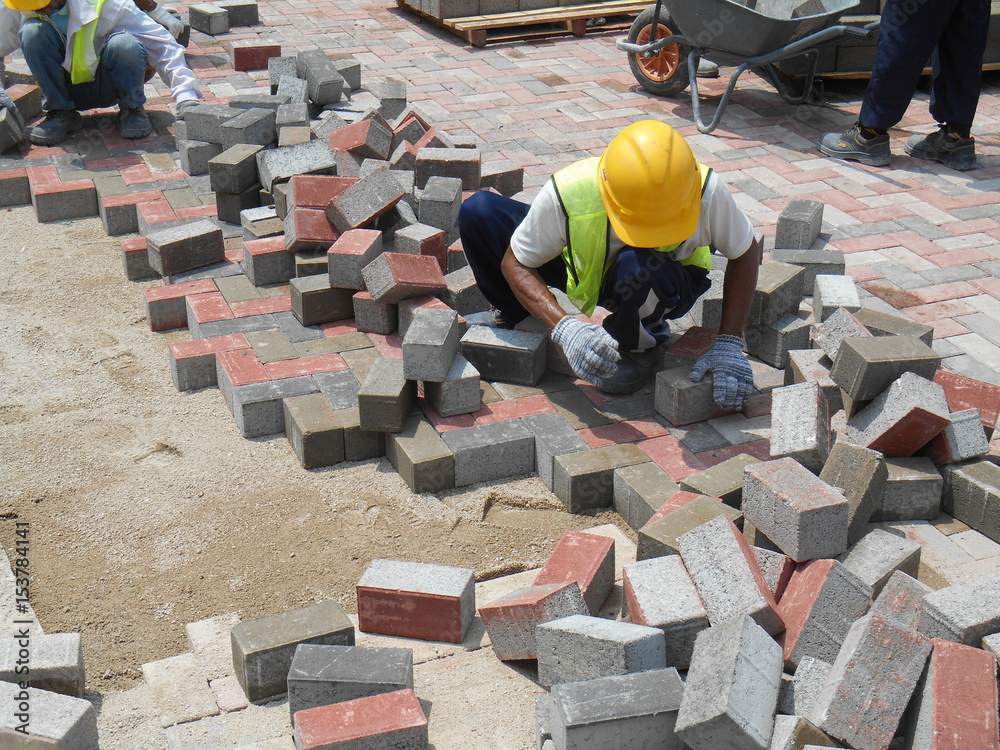 Construction workers installing and arranging precast concrete pavers ...