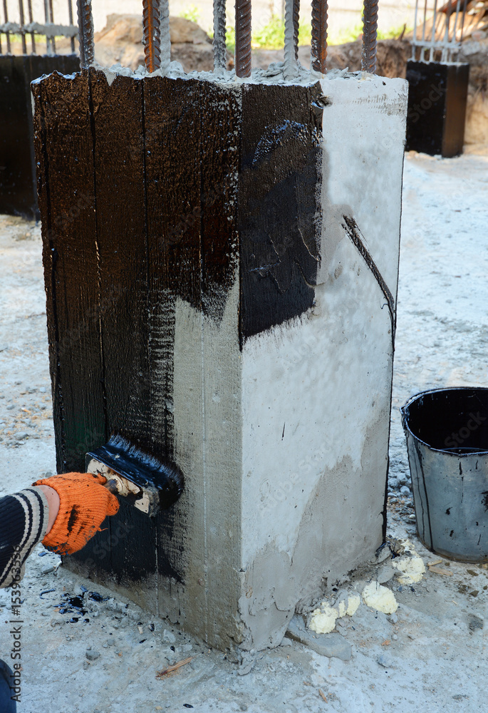 Builder worker painting black coal tar or bitumen at concrete surface ...