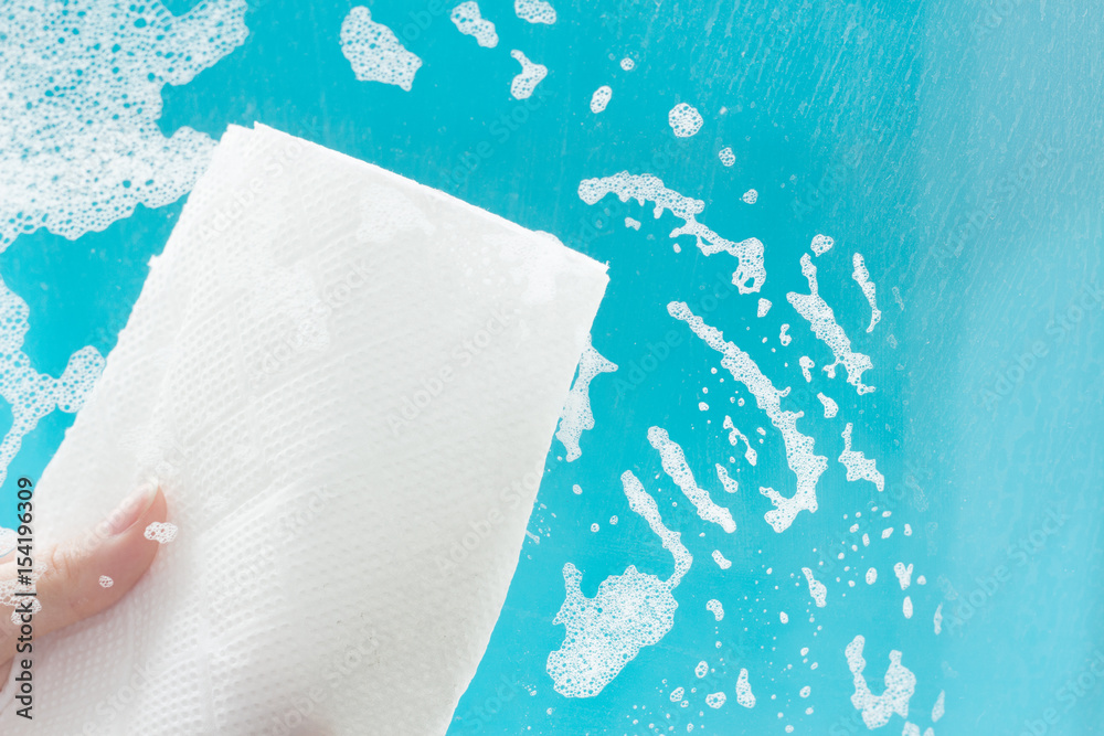 Female hand cleaning window with paper towel and detergent on blue ...