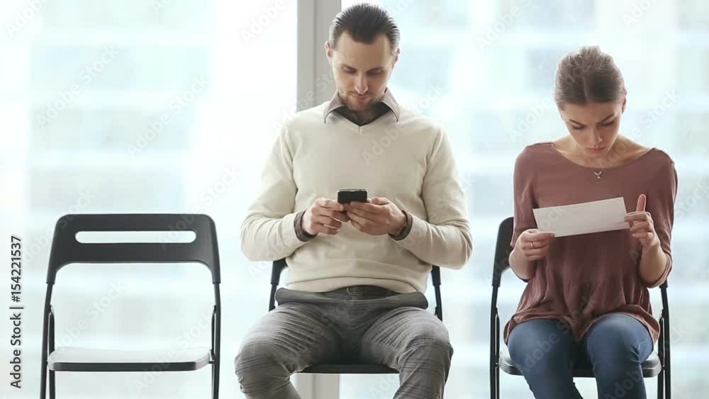 Two young applicants waiting their turn for job interview on chairs in ...