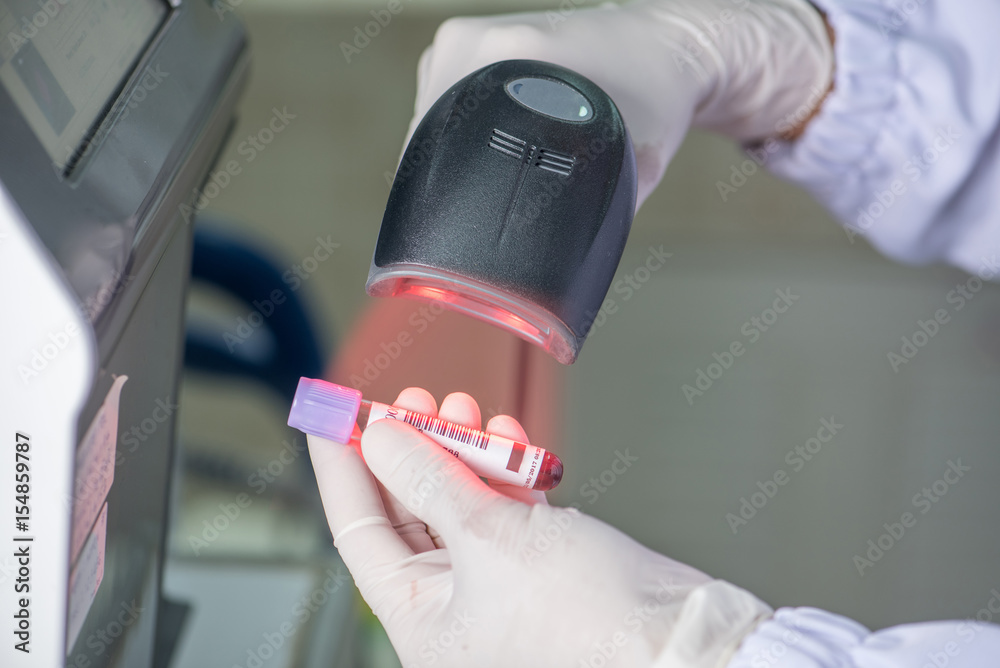 Technician scanning bar codes on biological sample tube in lab of blood ...