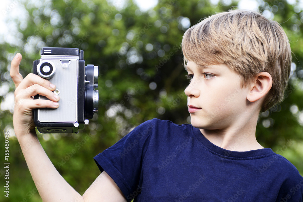 Little child blond boy with an old camera shooting outdoor. Kid taking ...