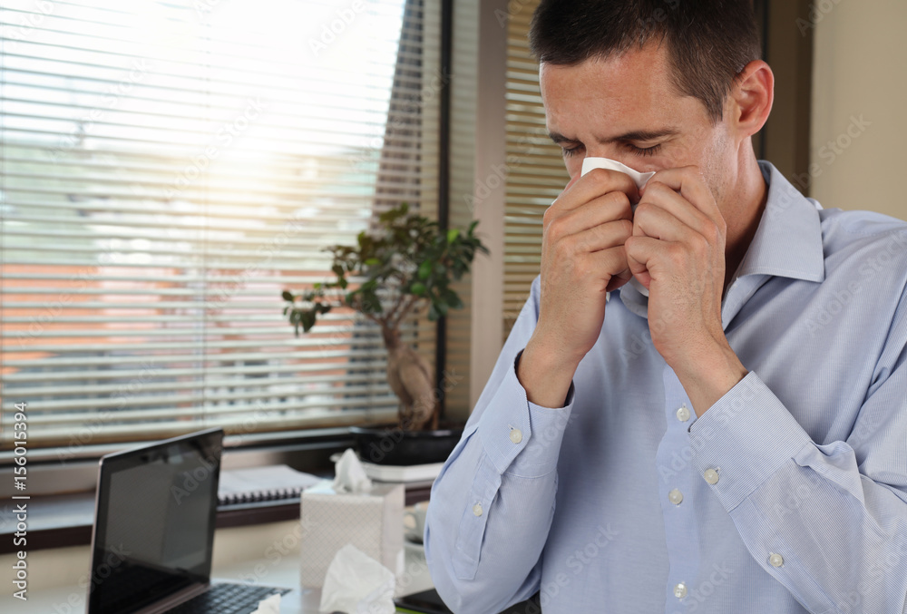 Business man with sneezing in a tissue in an office / workplace. Pollen ...