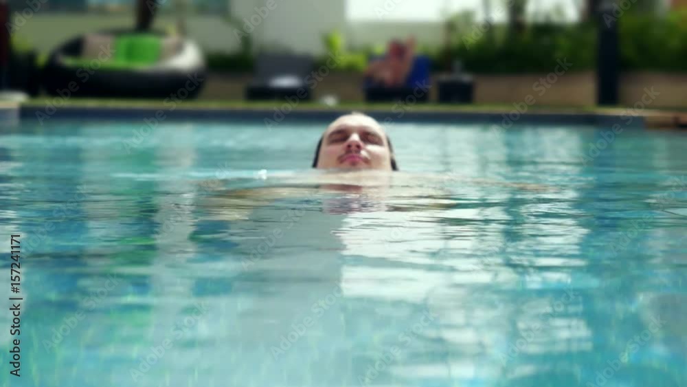 Bearded fat young man swims on back along city view in swimming pool ...