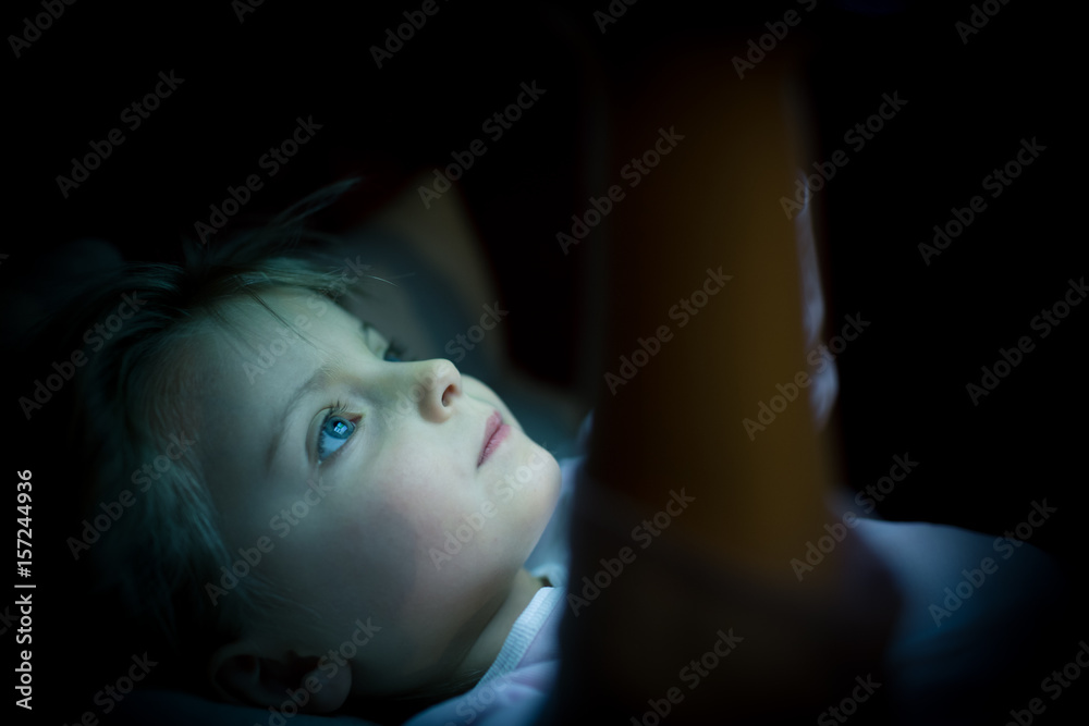 little child girl using tablet technology in bed by night at home ...