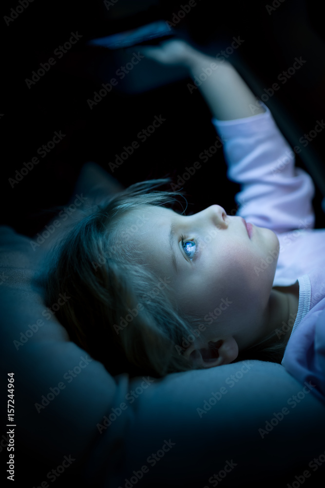 little child girl using tablet technology in bed by night at home ...