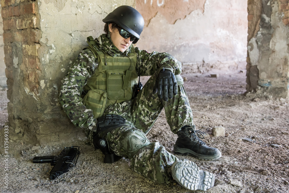 The soldier sits leaning against a wall in a ruined building. Military ...