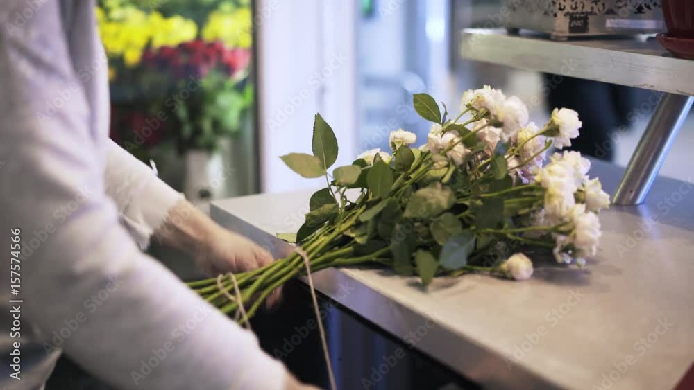 Close up of woman florist hans threading a bunch of white roses lying ...