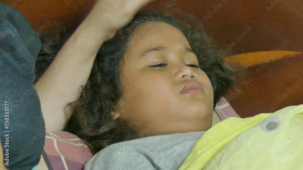 An Asian girl with the flu groans as her mother takes care of her ...