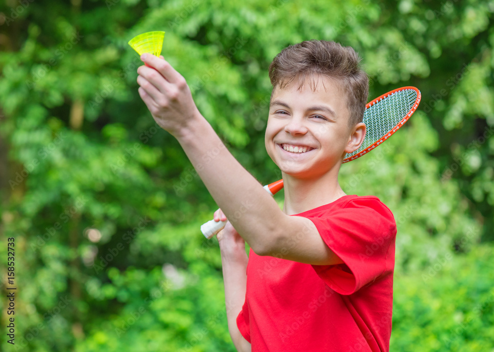 Young teen boy playing badminton in meadow with forest in background ...