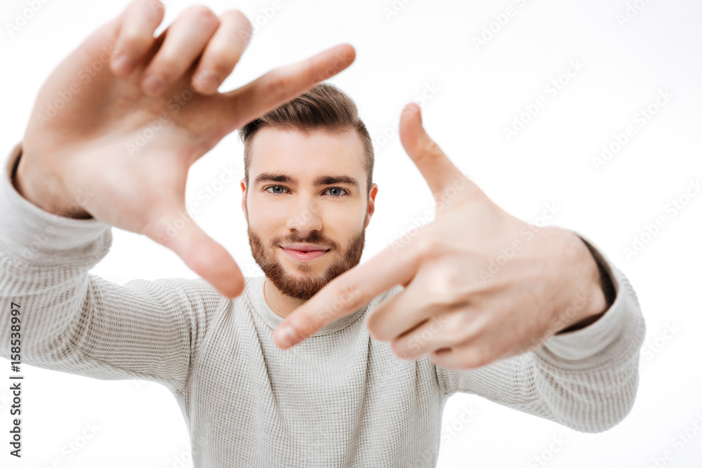 Young man making finger frame as a director of photography and smilibg over white background ...