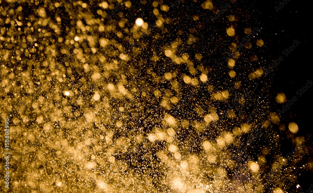 Sparkling golden glitter particles floating and glowing in motion against a dark background ...