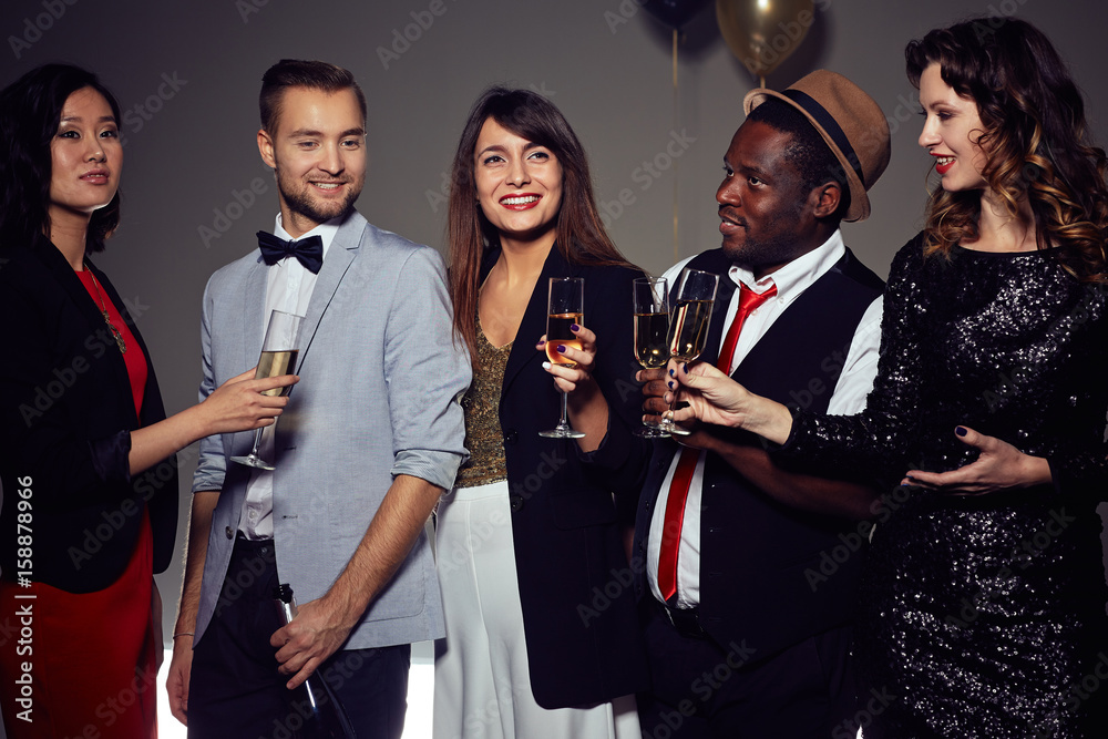 Group of smiling friends wearing trendy clothes standing against dark ...