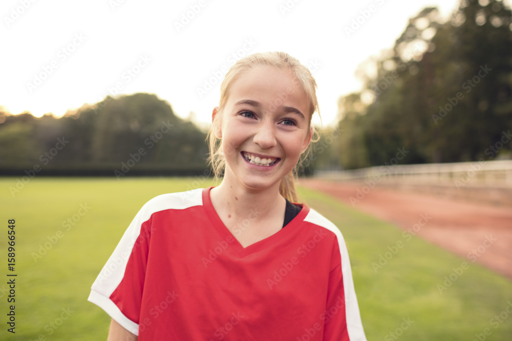 Happy girl wearing red sports uniform standing on soccer field against ...