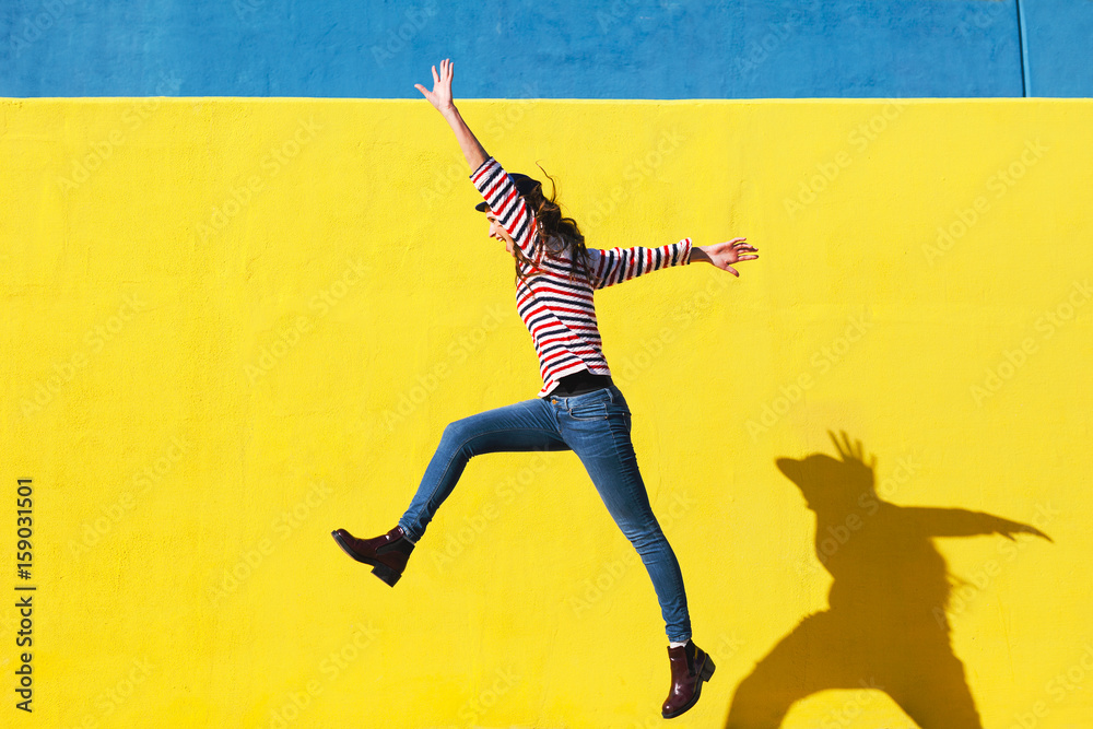 Happy woman jumping in front of yellow background Stock Photo | Adobe Stock