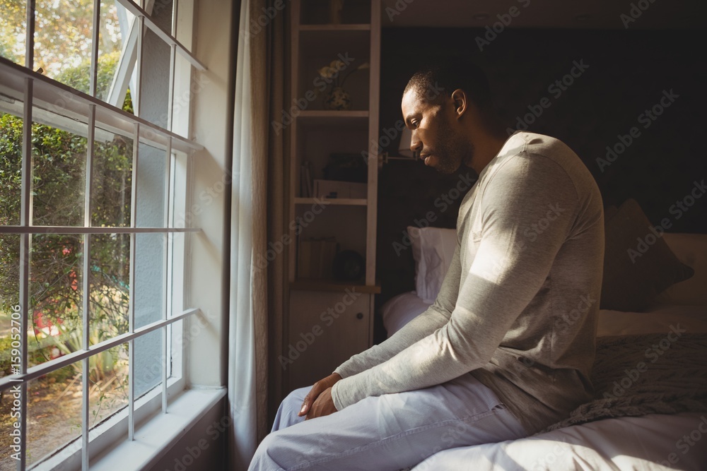 Side view of sad man sitting on bed by window Stock Photo | Adobe Stock