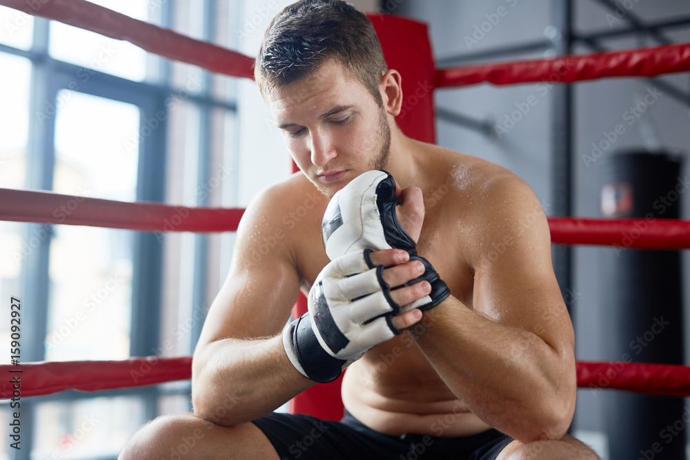 Portrait of sweaty shirtless man sitting in boxing ring and adjusting ...